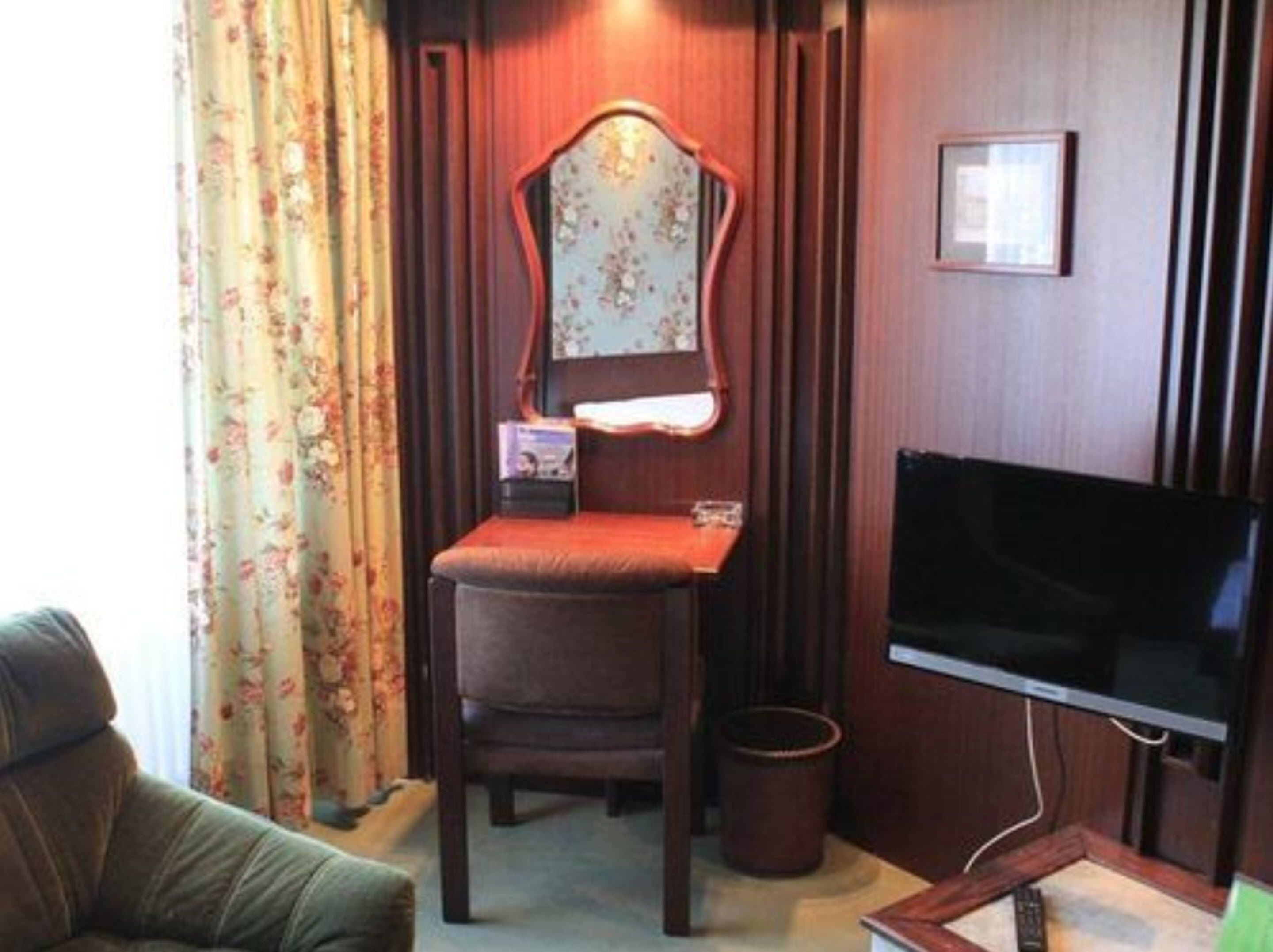 Quarto com escrivaninha de madeira, uma cadeira, televisão e lixeira.