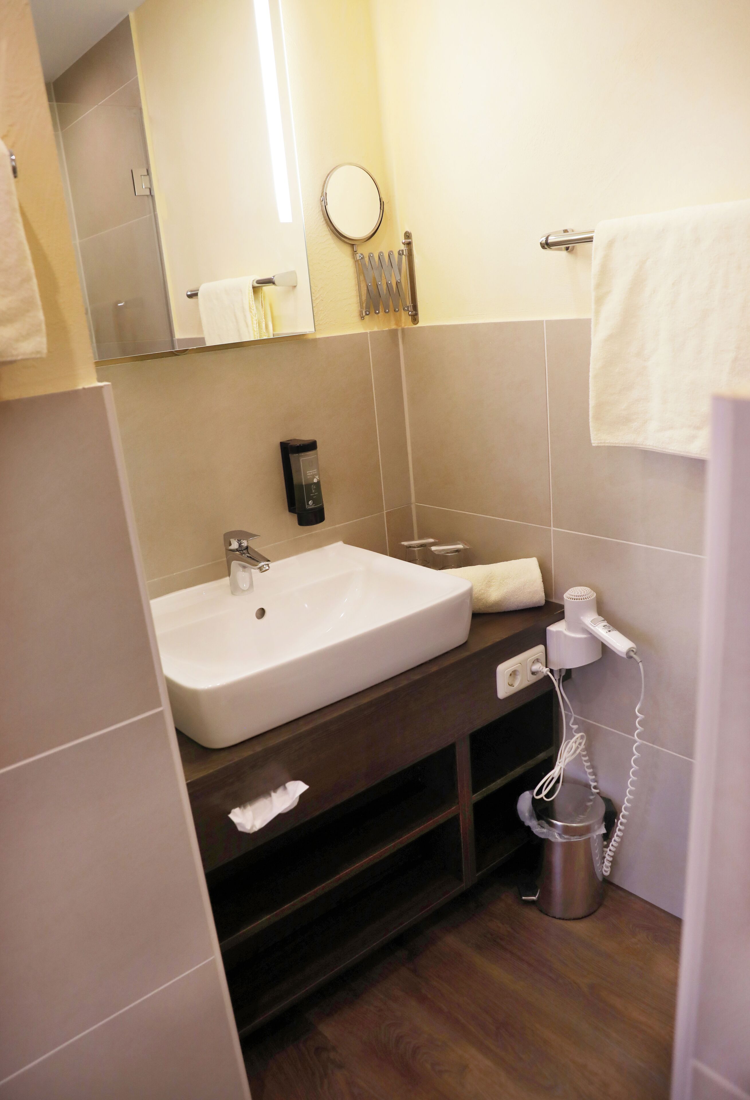 Casa de banho com lavatório branco, espelho, porta-toalhas e secador de cabelo.