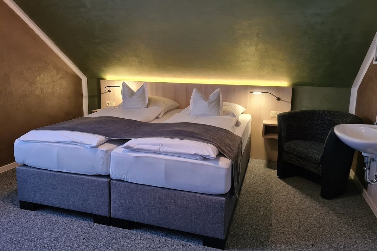 Quarto de hotel com cama, mesa de cabeceira, cadeira e pia.
