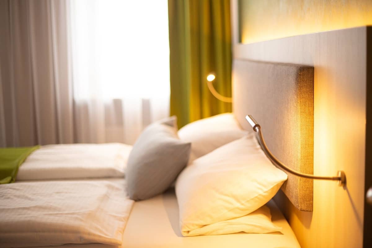 Quarto de hotel com cama, almofadas e cabeceira com luminária.