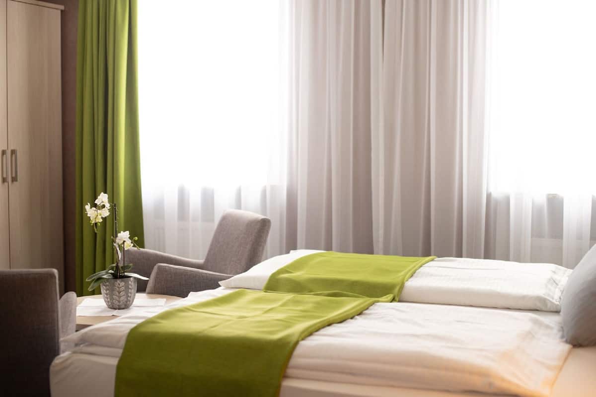 Quarto de hotel com cama, uma cadeira, uma mesa com planta e janela com cortinas.