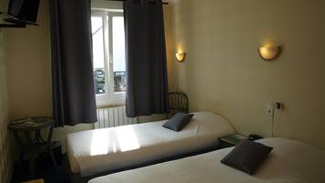 Quarto de hotel com duas camas, uma mesa pequena, uma cadeira, uma televisão e uma janela com cortinas.