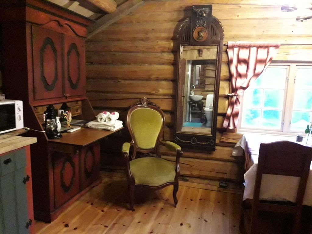 Interior de cabana de tronco com mesa de jantar de madeira, uma cadeira estofada verde, um armário de madeira e um espelho grande.
