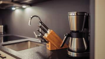 Cozinha moderna com cafeteira de aço inoxidável, porta-facas de madeira e bancada preta.