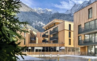 Um edifício moderno com várias varandas, fachada de madeira e vista para montanhas cobertas de neve.