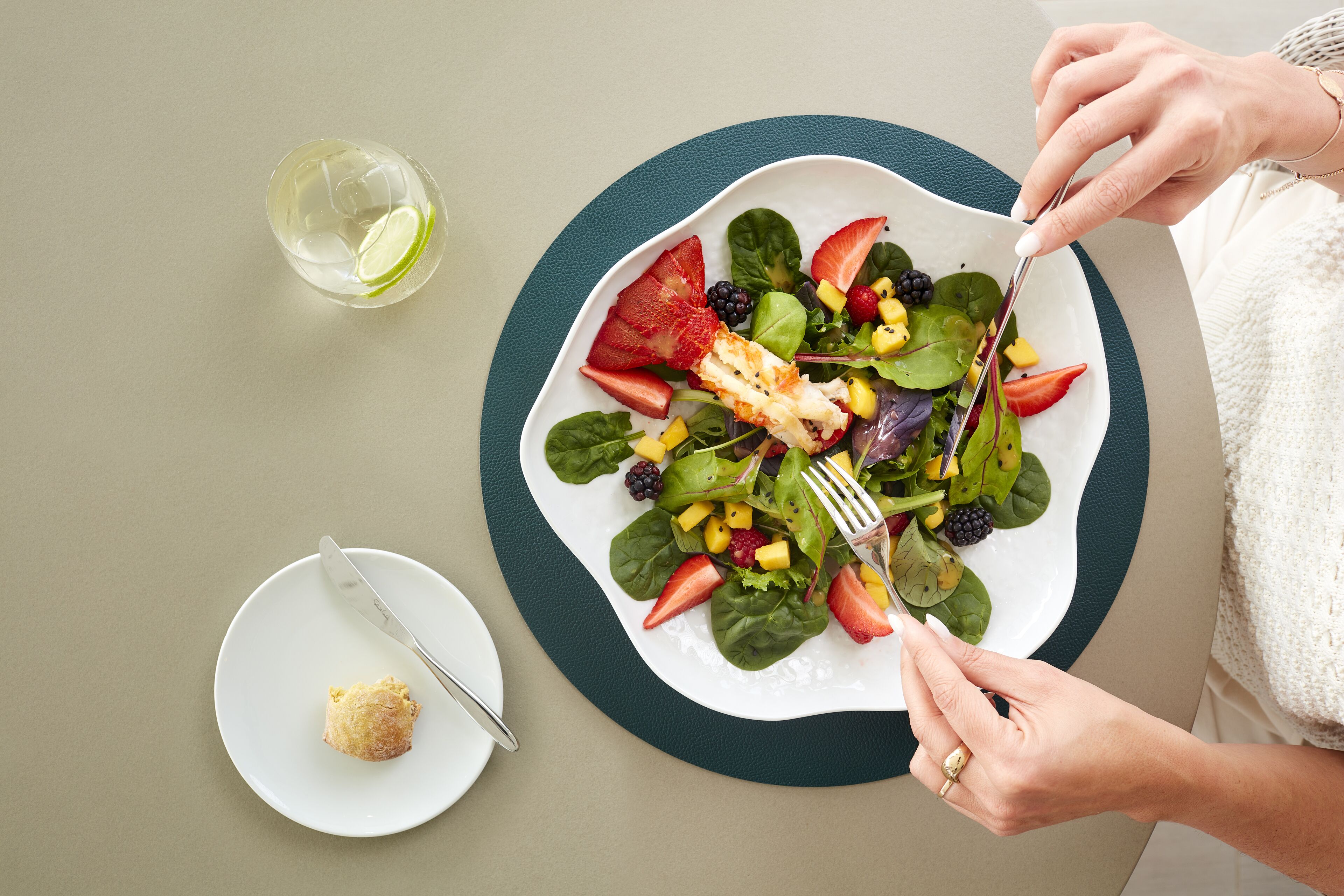 Uma mesa de jantar com uma salada num prato, um copo de água e um biscoito numa pequena travessa.