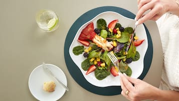 Uma mesa de jantar com uma salada num prato, um copo de água e um biscoito numa pequena travessa.