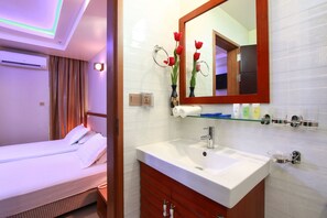 Quarto de hotel com uma cama, banheiro com pia, espelho e artigos de higiene pessoal.