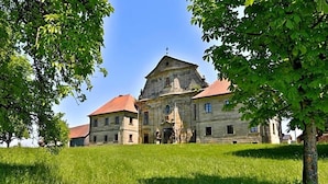 Um edifício histórico de pedra com telhado vermelho, rodeado por relva verde exuberante e árvores.