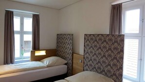 Quarto de hotel com duas camas, uma janela com cortinas e um radiador.