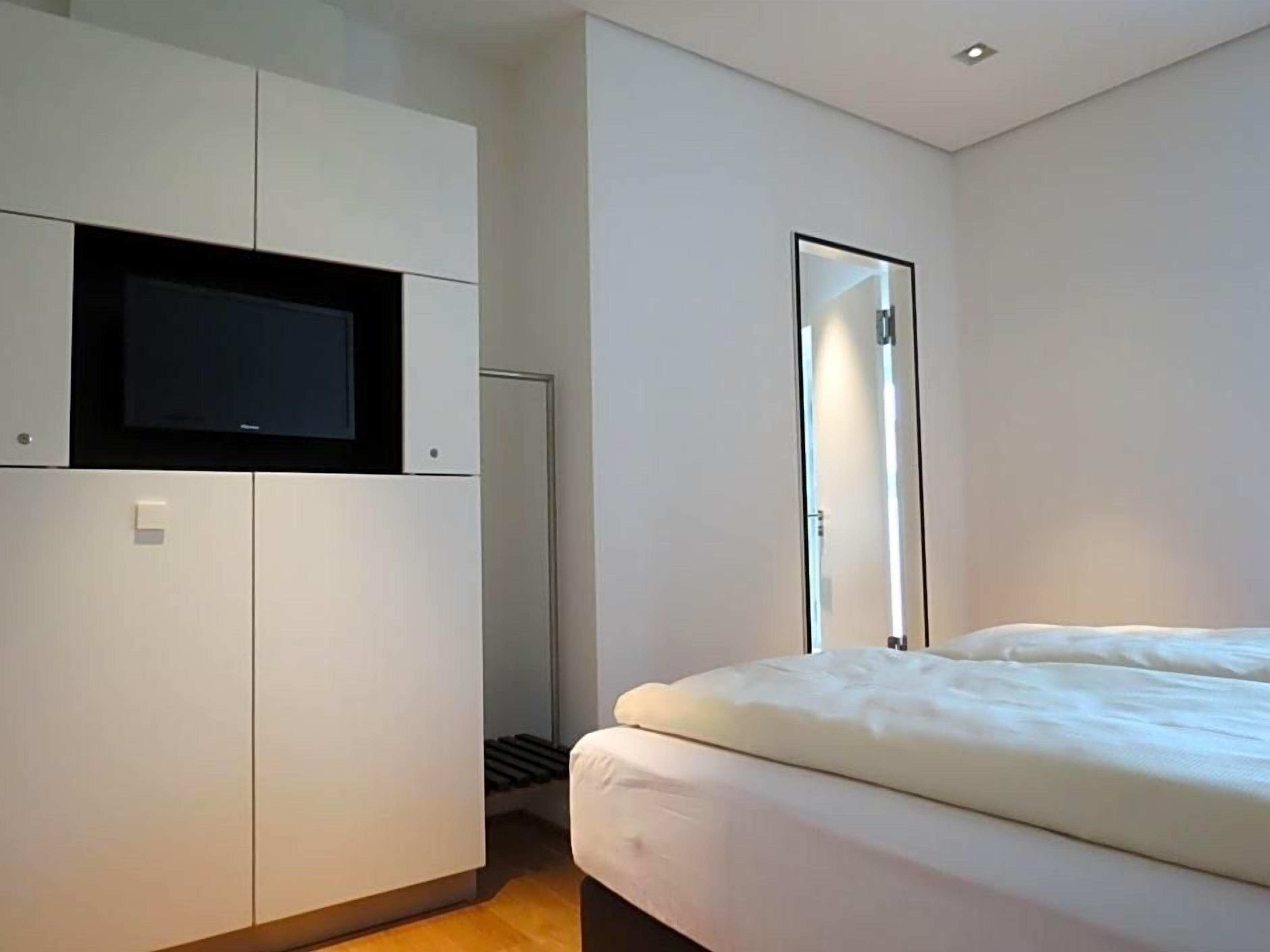 Quarto com cama, televisão fixada em um móvel e espelho na parede.
