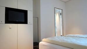 Quarto com cama, televisão fixada em um móvel e espelho na parede.