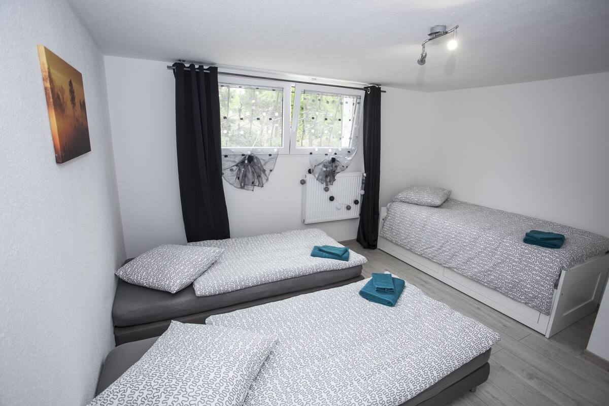 Quarto com duas camas, um radiador, uma janela com cortinas e um quadro na parede.