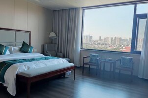 Quarto de hotel com uma cama grande, uma escrivaninha, duas cadeiras e vista para a cidade.