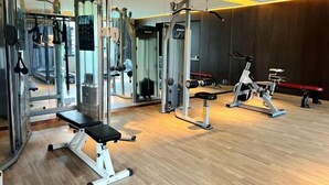 Academia com diversos equipamentos de exercício, incluindo um banco, aparelhos de musculação e um remo.