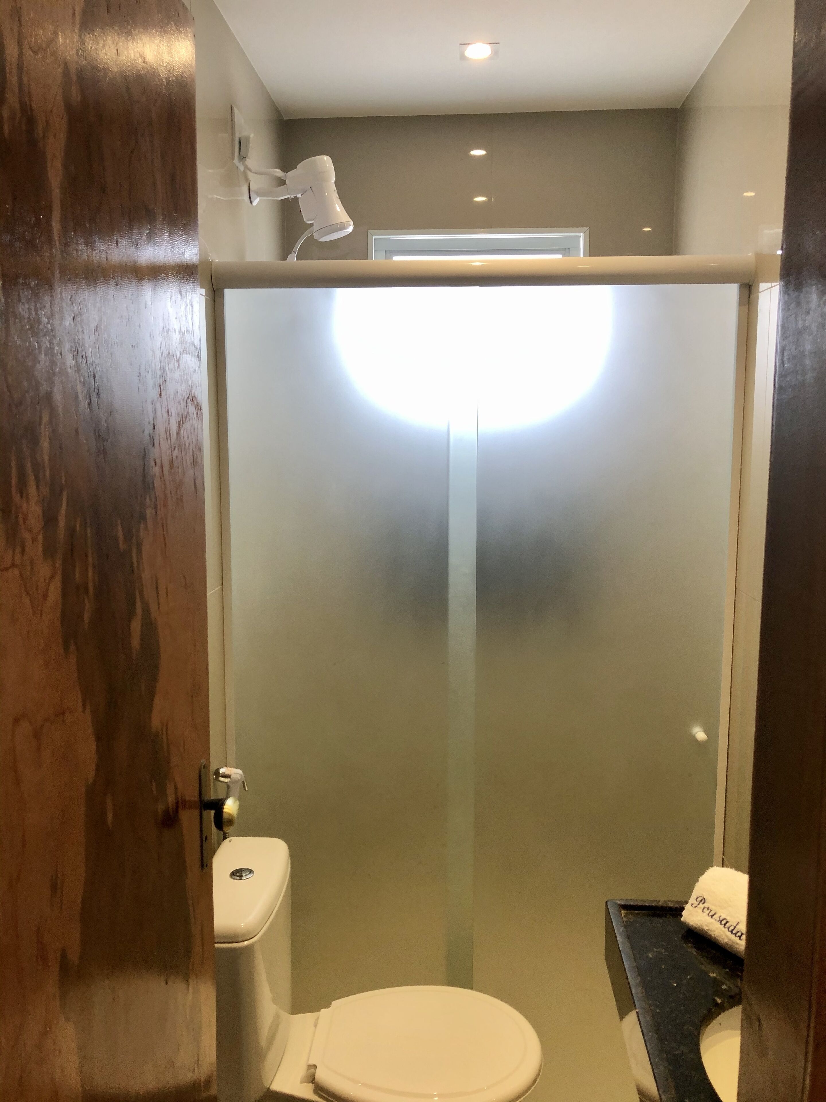 Um banheiro com vaso sanitário branco, chuveiro com box de vidro, porta-toalhas e pia com toalha.