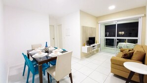 Uma sala de estar moderna com área de jantar, sofá, televisão e varanda com mesa.