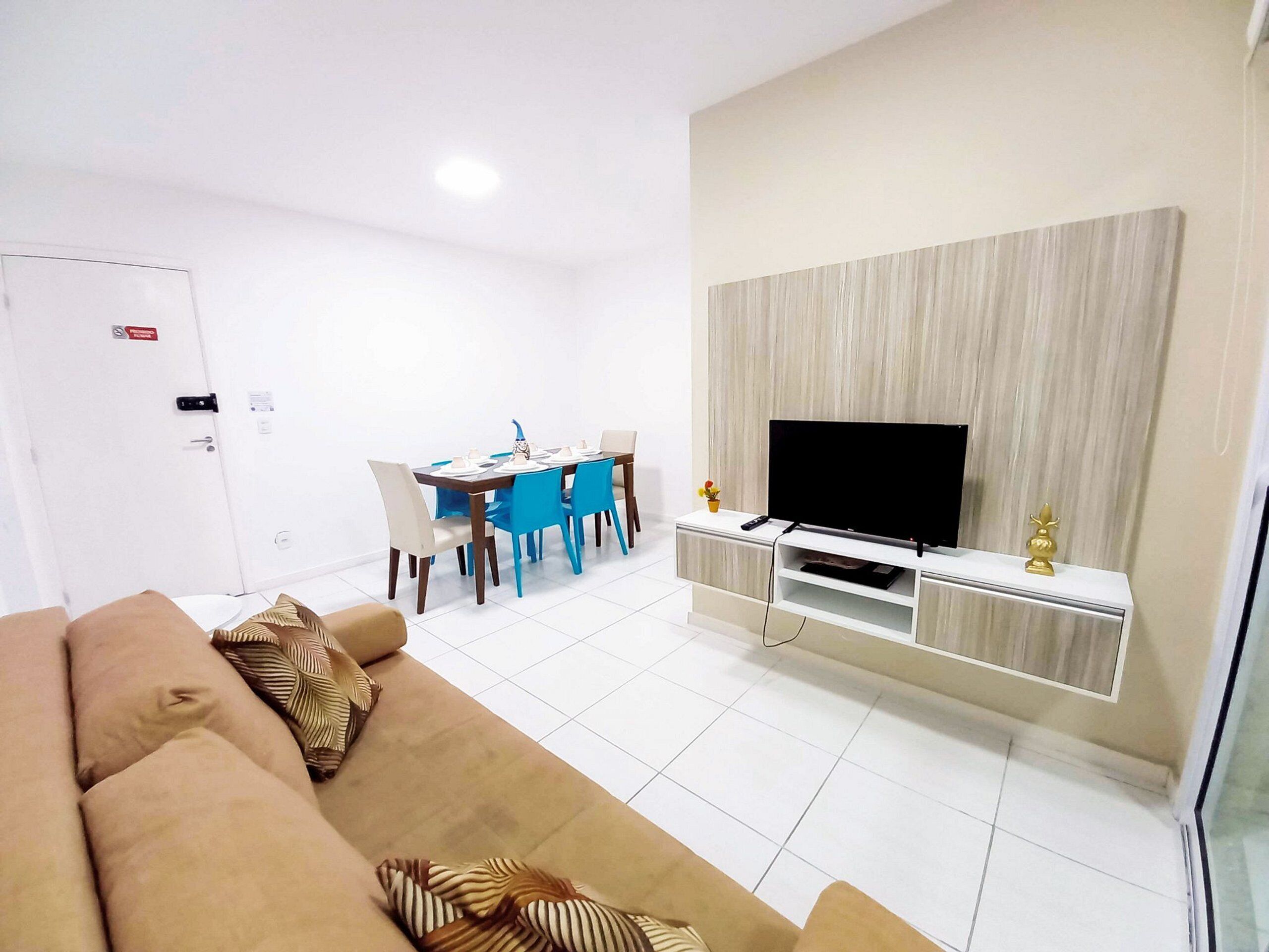 Sala de estar com sofá, televisão e área de jantar com cadeiras e mesa.