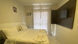 Quarto de hotel com cama, televisão na parede e janela com cortinas.
