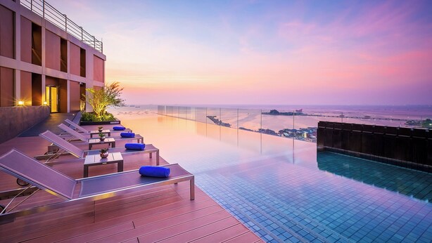 Piscina infinita no terraço com espreguiçadeiras e vista para o horizonte da cidade ao pôr do sol.