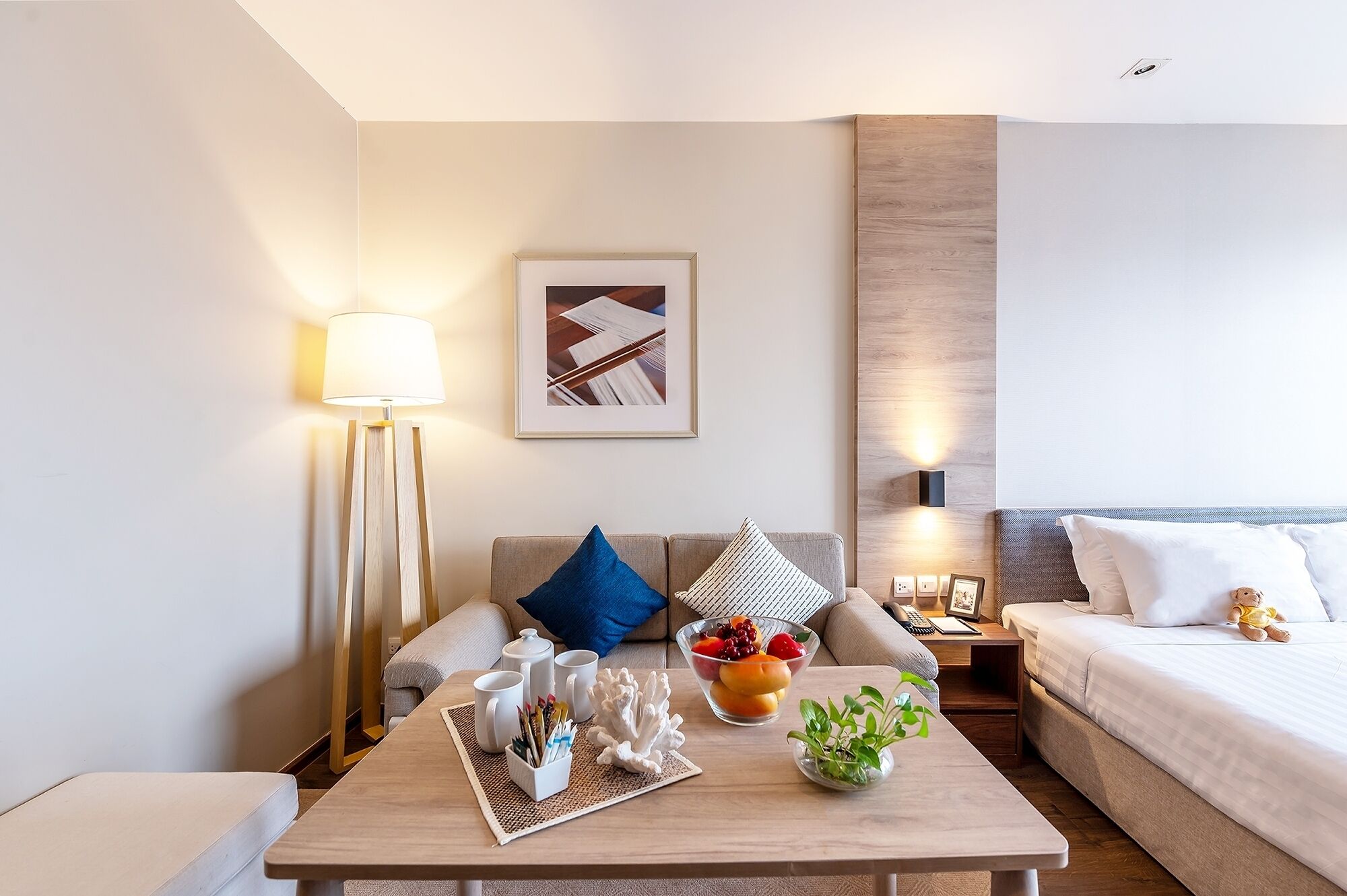 Quarto de hotel moderno com sofá, uma pequena mesa com uma cesta de frutas, luminária e cama.