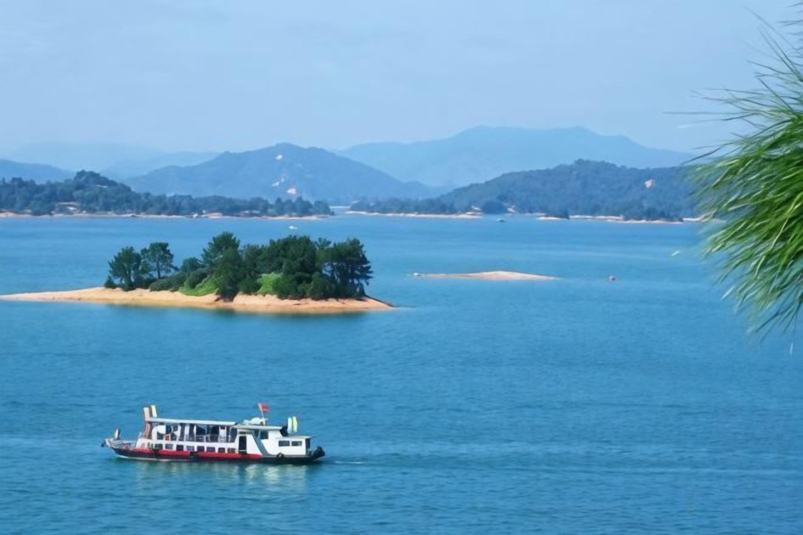 Um barco em águas calmas, com uma pequena ilha e montanhas ao fundo.