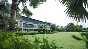 Um edifício moderno com telhado plano, cercado por gramado bem cuidado e palmeiras.