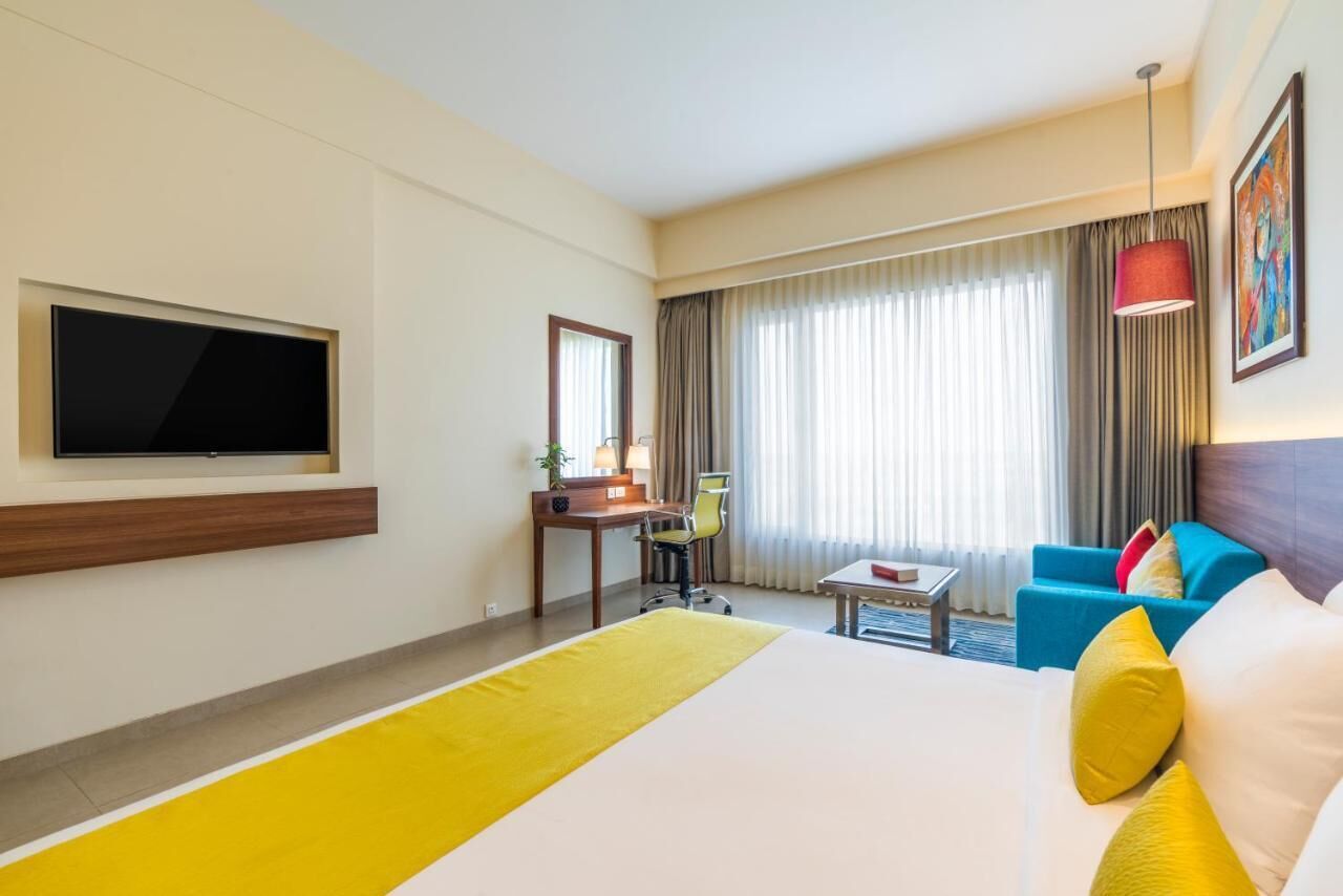 Quarto de hotel com cama, escrivaninha, cadeira, televisão e sofá.