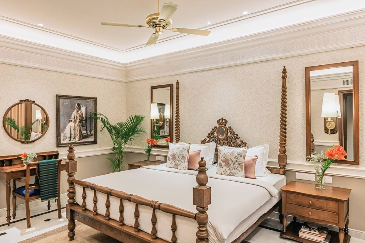 Quarto com cama de madeira, escrivaninha, cadeira, mesa de cabeceira e ventilador de teto.