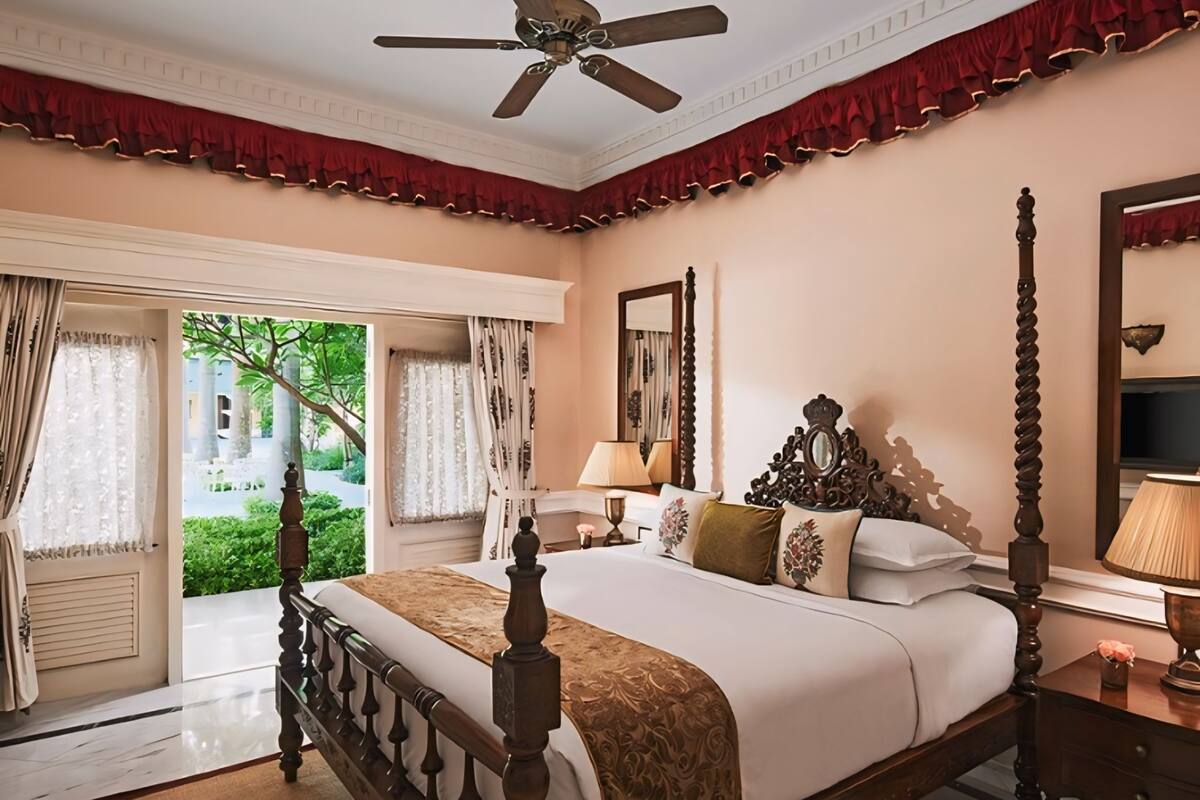 Quarto com cama grande, ventilador de teto, mesa de cabeceira, luminária e vista para o verde lá fora.