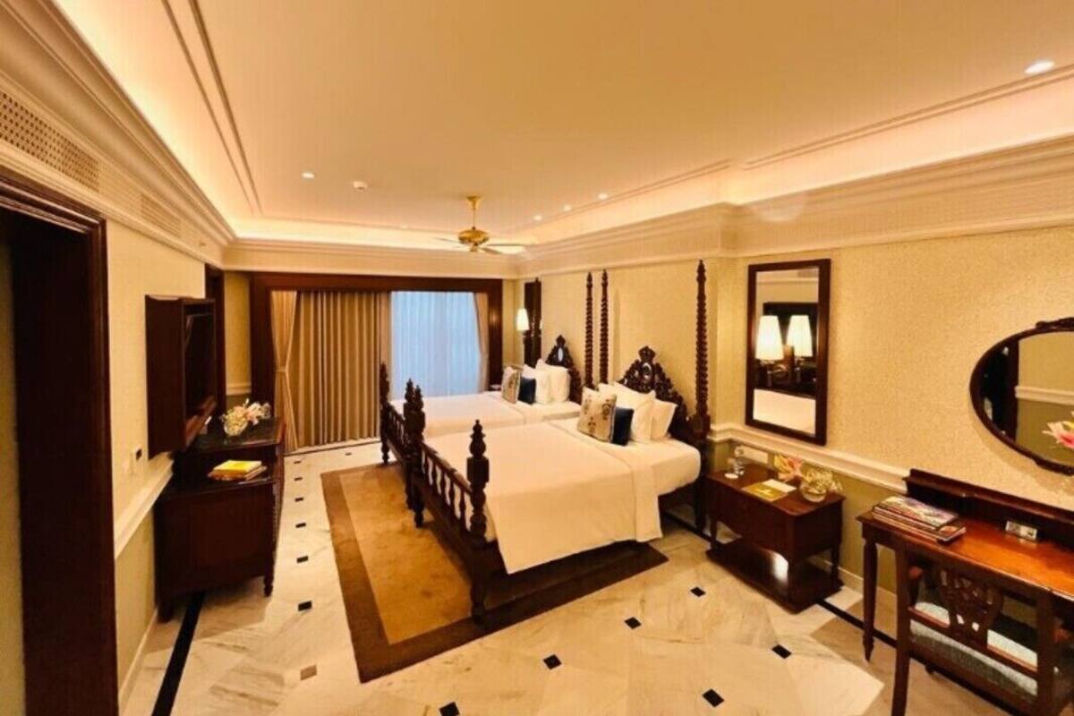 Quarto de hotel com uma cama grande, uma escrivaninha, uma cadeira, um espelho e uma janela com cortinas.