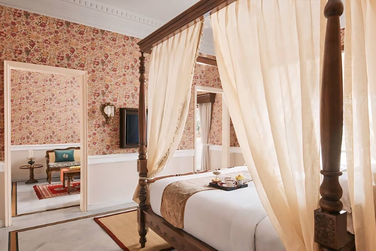 Uma cama de dossel com cortina, um espelho, uma mesinha com abajur e uma parede com padrão floral.