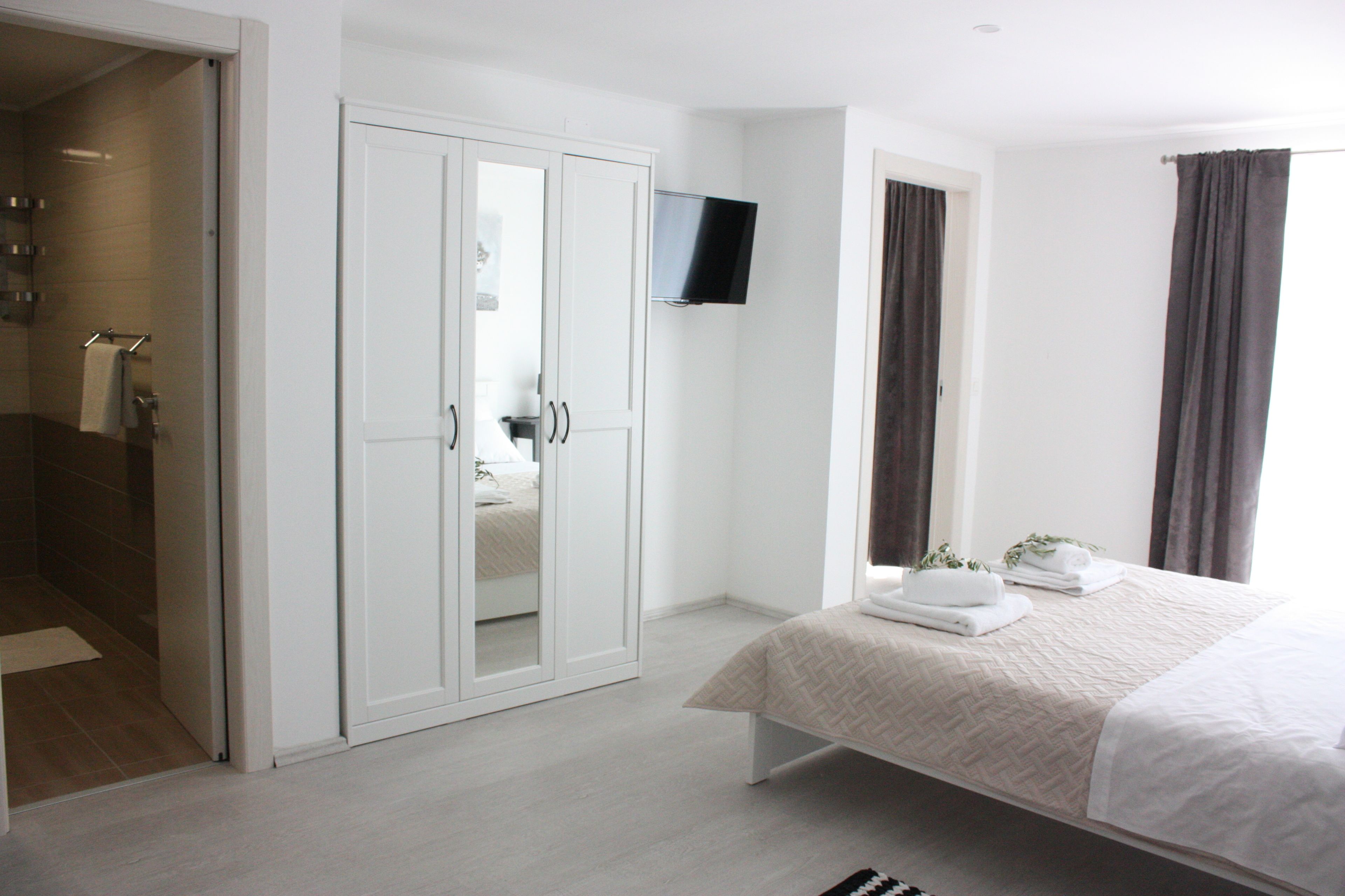 Quarto moderno com cama, guarda-roupa, televisão e zona de chuveiro.
