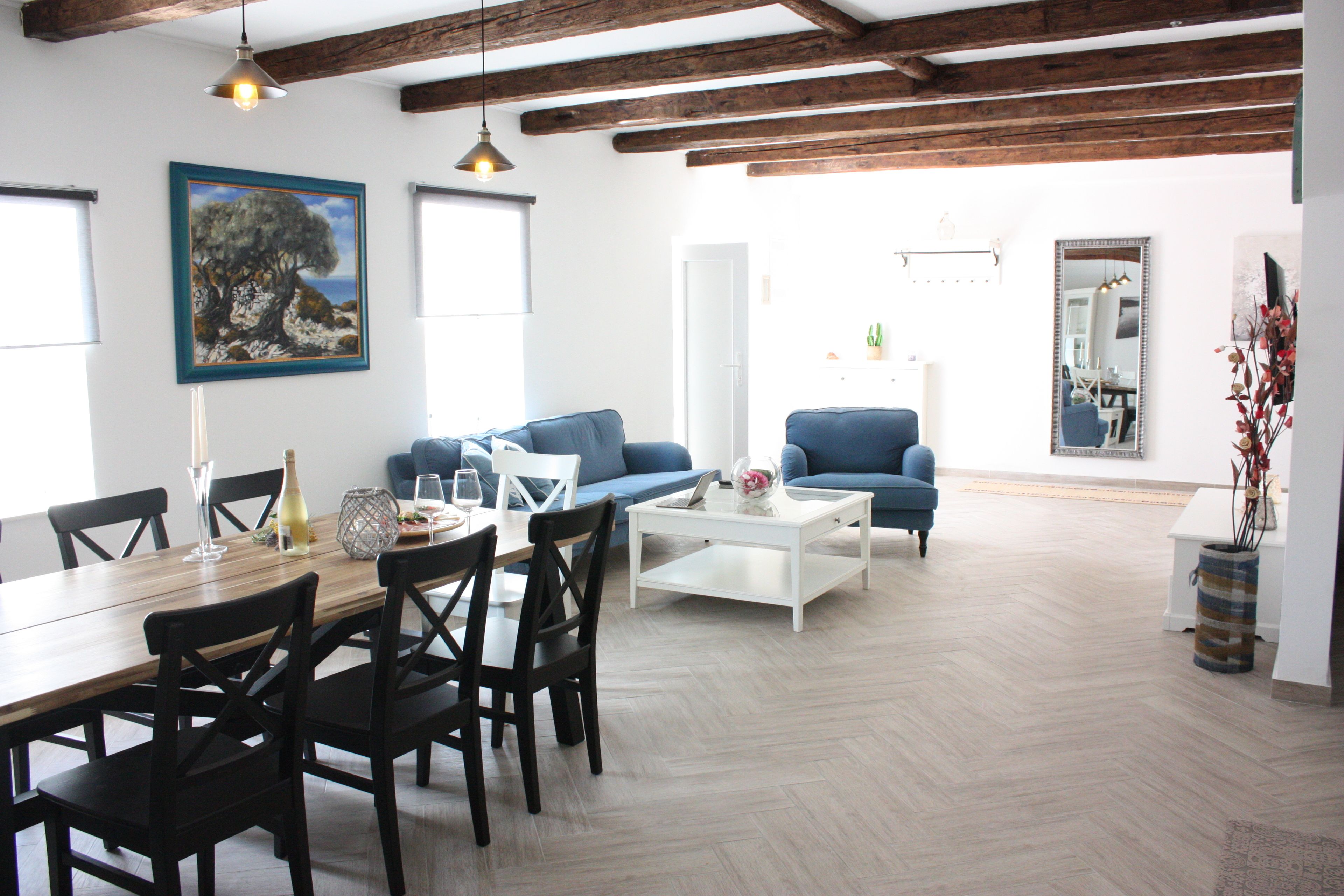 Uma sala de estar moderna com uma mesa de jantar de madeira, sofás azuis e uma mesa de centro branca.