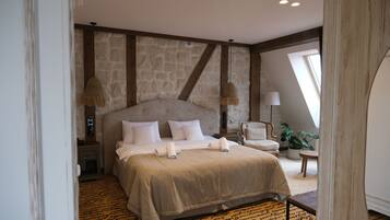 Quarto com parede de pedra, uma cama grande com roupa de cama branca, cabeceira de madeira e duas luminárias pendentes.