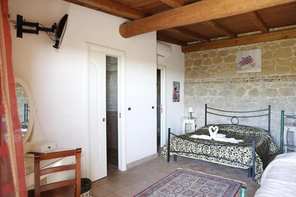 Quarto com cama, cadeira, espelho, porta e parede de pedra.