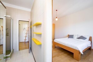 Quarto com cama de madeira, uma pequena mesa de cabeceira e uma prateleira na parede.