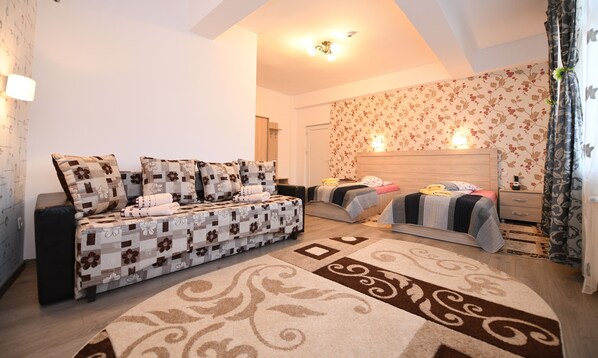 Quarto com sofá, duas camas, cabeceira de madeira e papel de parede estampado com flores.