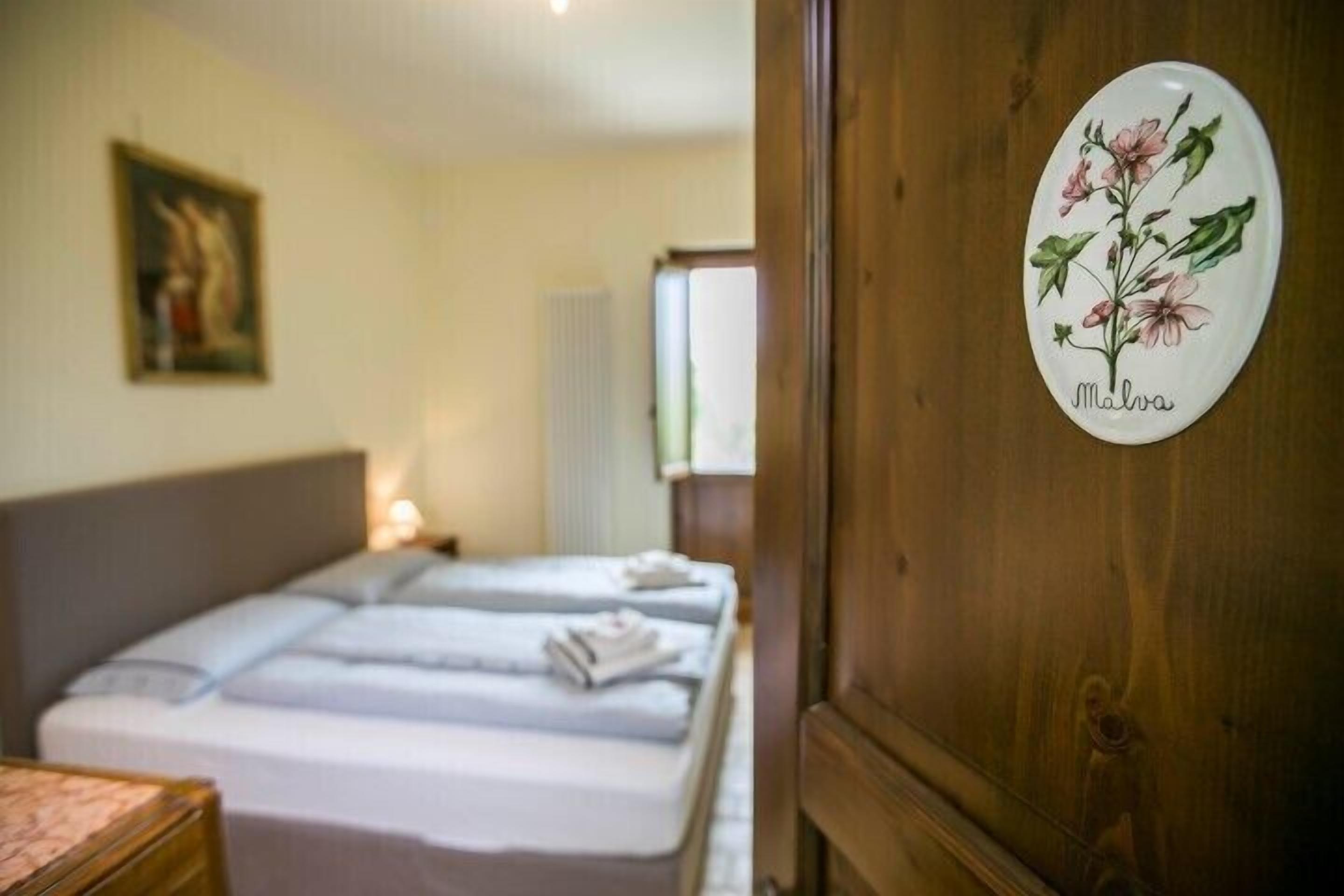 Quarto de hotel com duas camas, porta de madeira e um adesivo floral na parede.