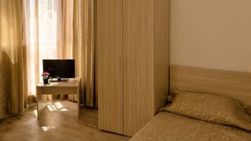 Quarto com guarda-roupa de madeira, cama com roupa de cama estampada, mesa pequena com televisão e um vaso de flores.