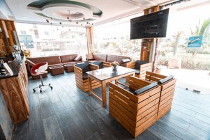 Uma área de estar moderna com mobiliário de madeira, uma mesa de vidro e uma TV fixada na parede.