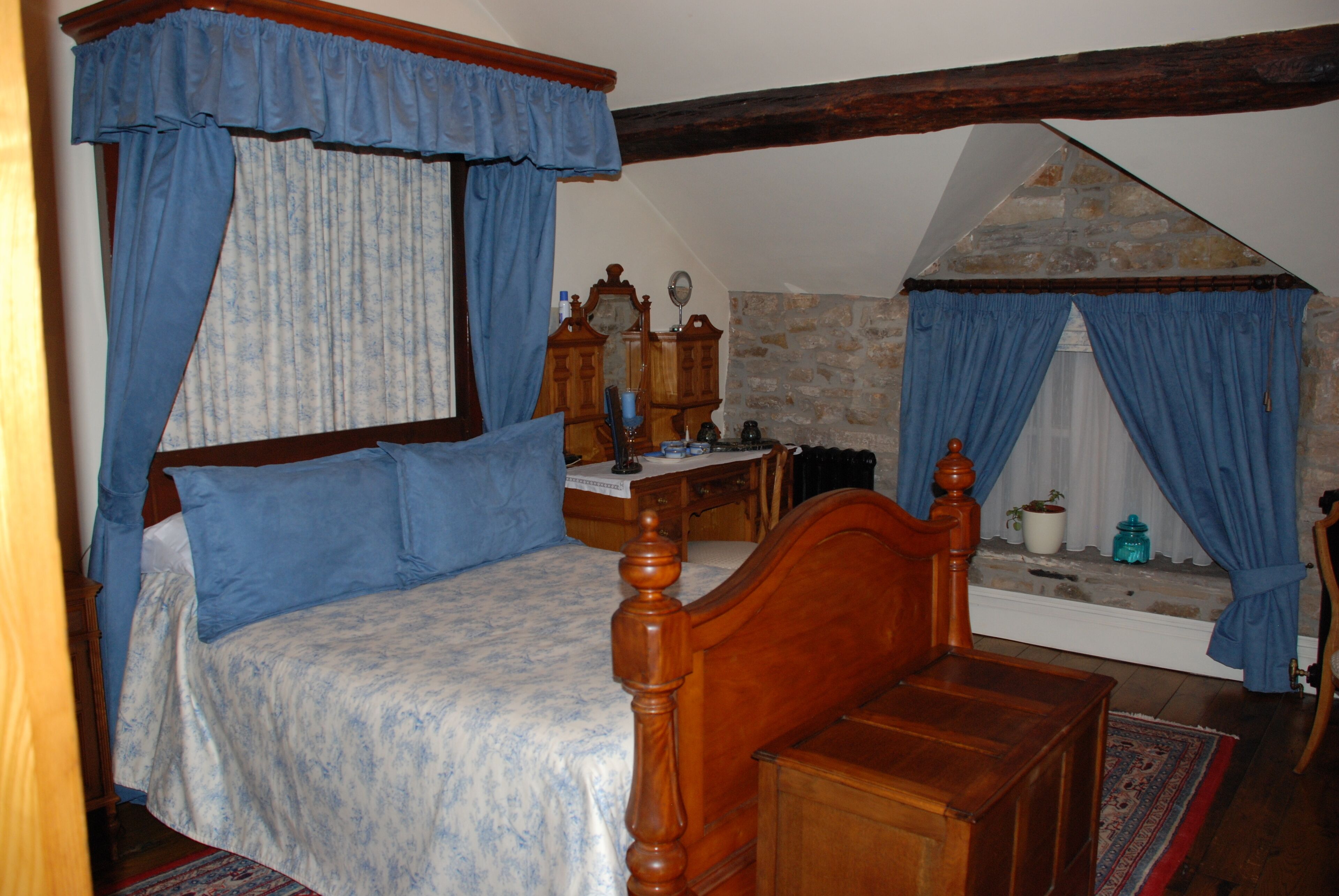 Um quarto com uma cama de madeira, uma mesa de cabeceira, um penteado e uma parede de pedra.