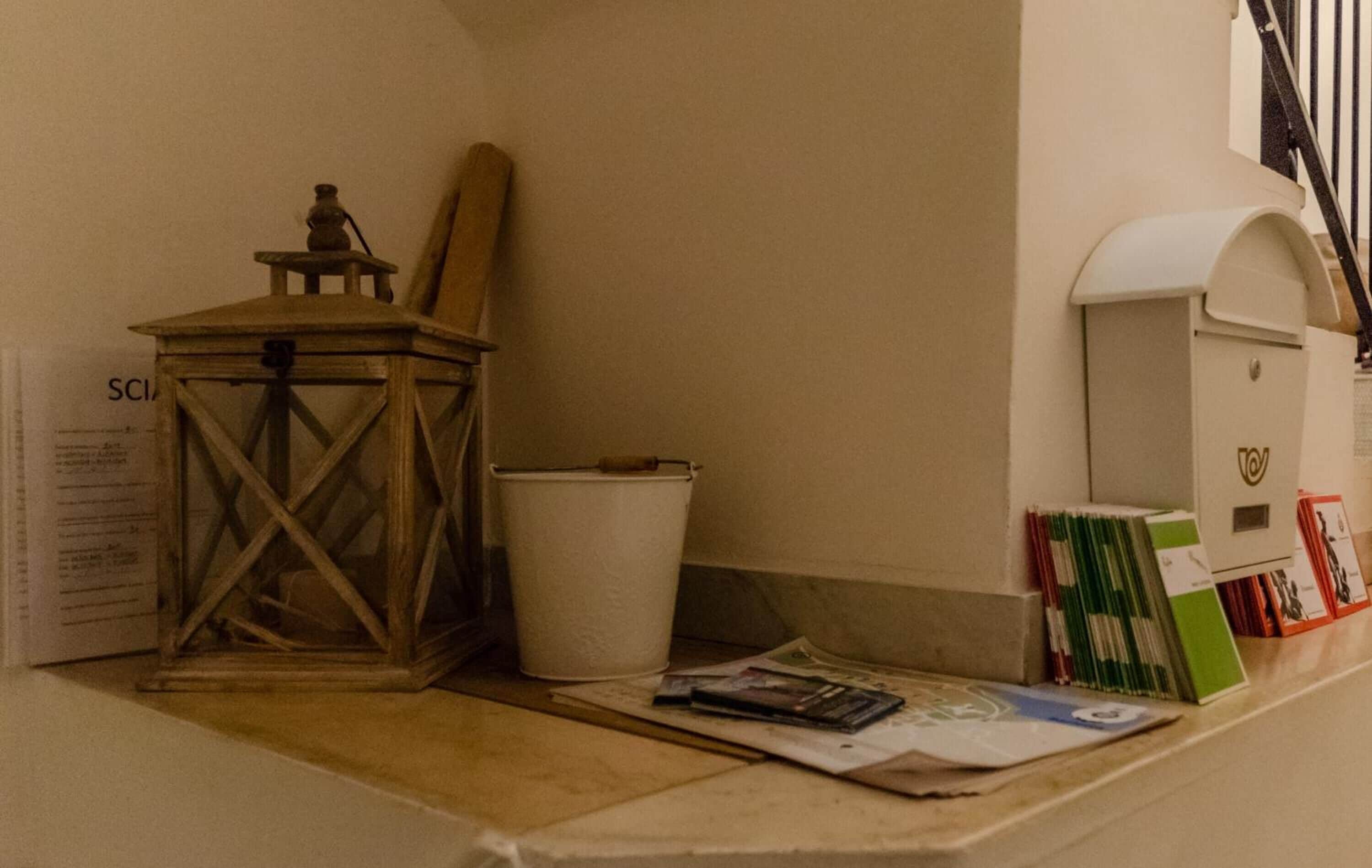 Canto com um candeeiro de madeira, uma lixeira branca e uma abertura para correspondência branca, com livros ao lado.