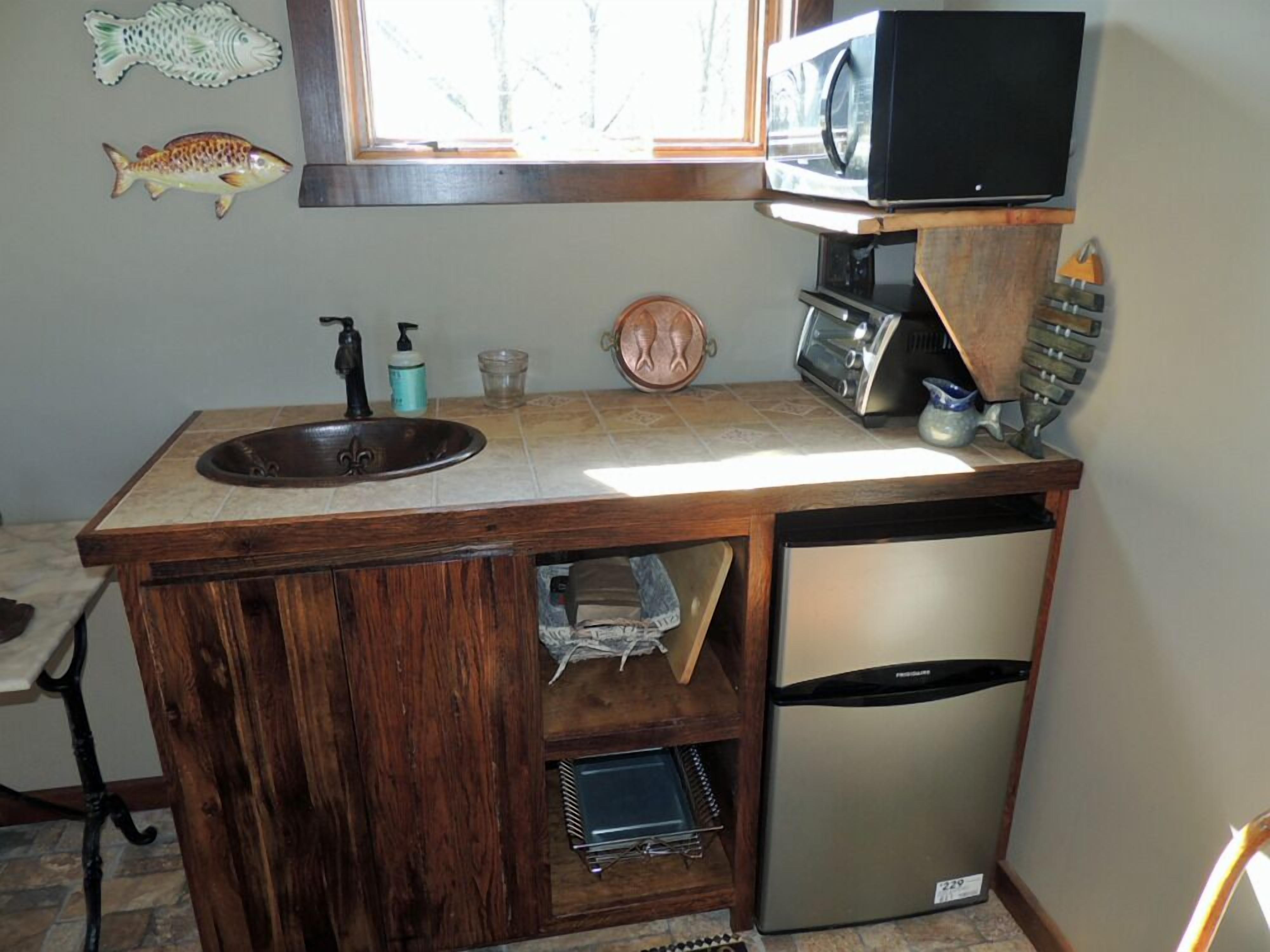 Cozinha compacta com bancada de madeira, pia, micro-ondas e geladeira.