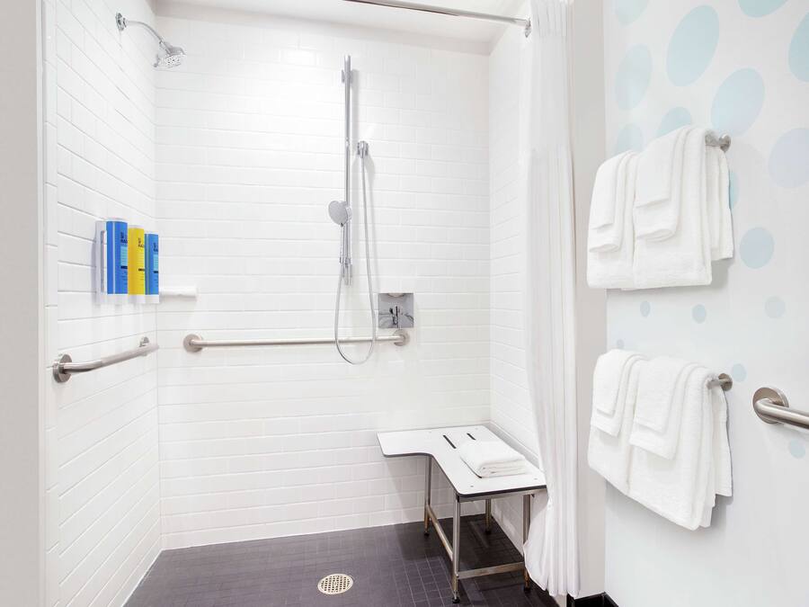 Um banheiro moderno com azulejos brancos estilo metrô, chuveiro com chuveiro manual, barra de apoio e porta-toalhas com vários toalhas.