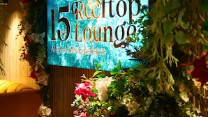 Placa para '15 Rcoftop Lounge', com um fundo de ripas de madeira verticais e decorações florais.