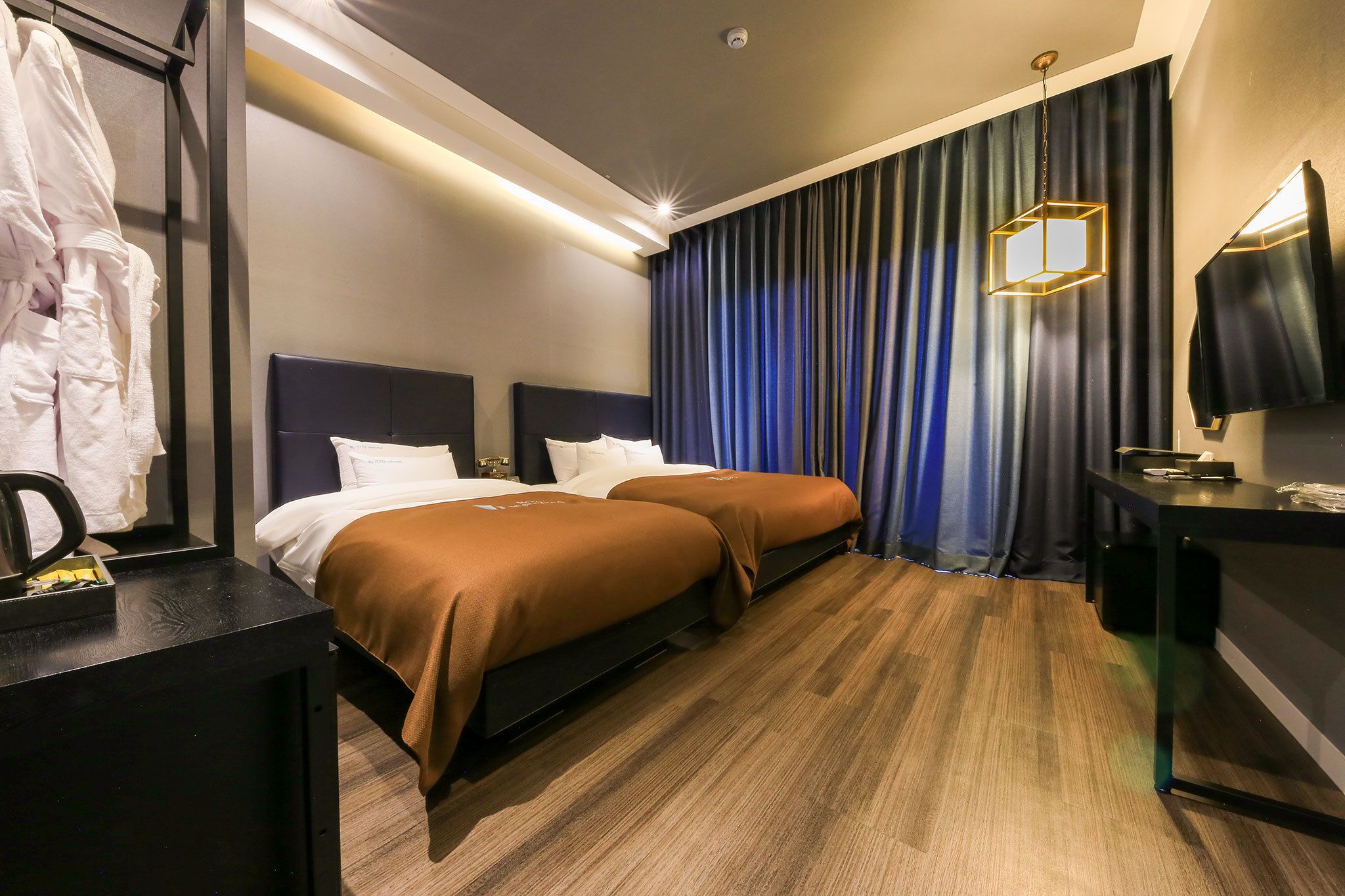 Quarto de hotel com duas camas, uma escrivaninha, um espelho, televisão e uma janela grande com cortinas.
