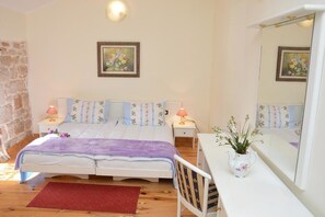 Quarto com cama, mesas de cabeceira, um espelho, tapete vermelho e um vaso com planta.