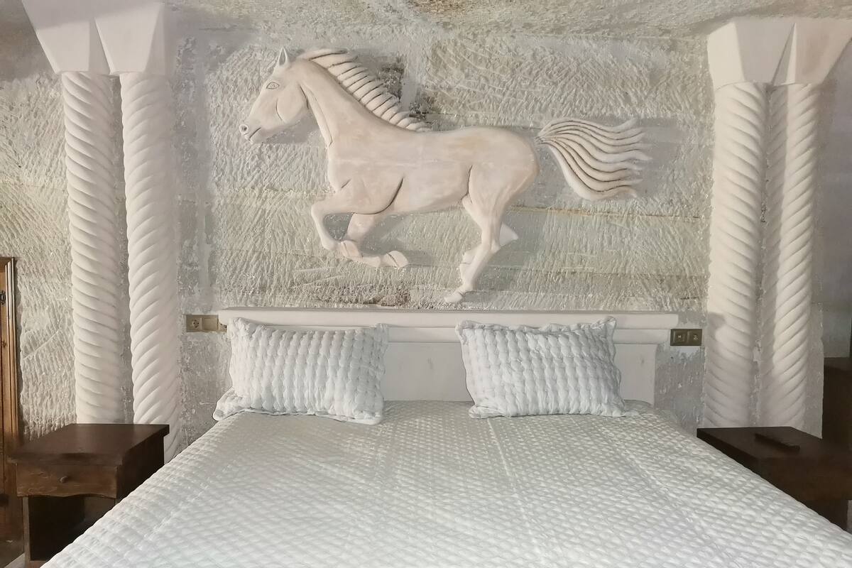 Quarto com uma cama grande, duas almofadas brancas e uma escultura de cavalo na parede.