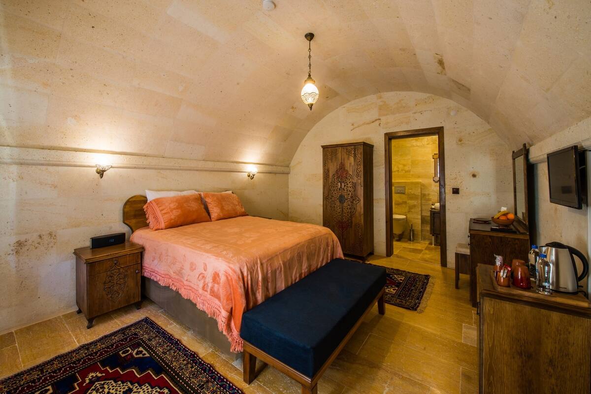 Quarto com cama, banco, mesa de cabeceira e guarda-roupa.